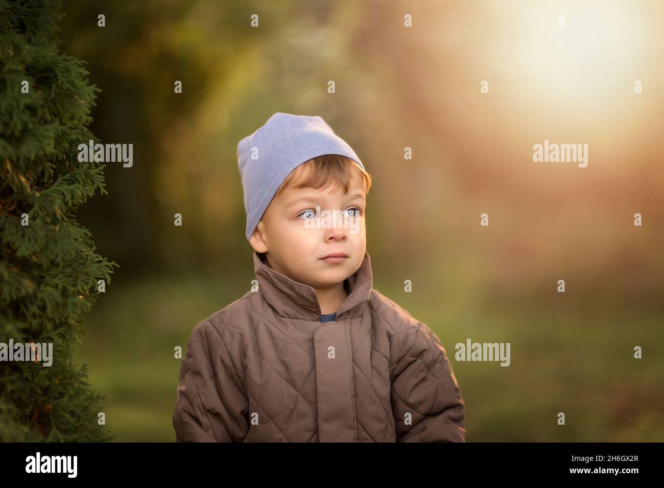 Portrait of sad boy standing in garden in beige jacket Stock Photo - Alamy