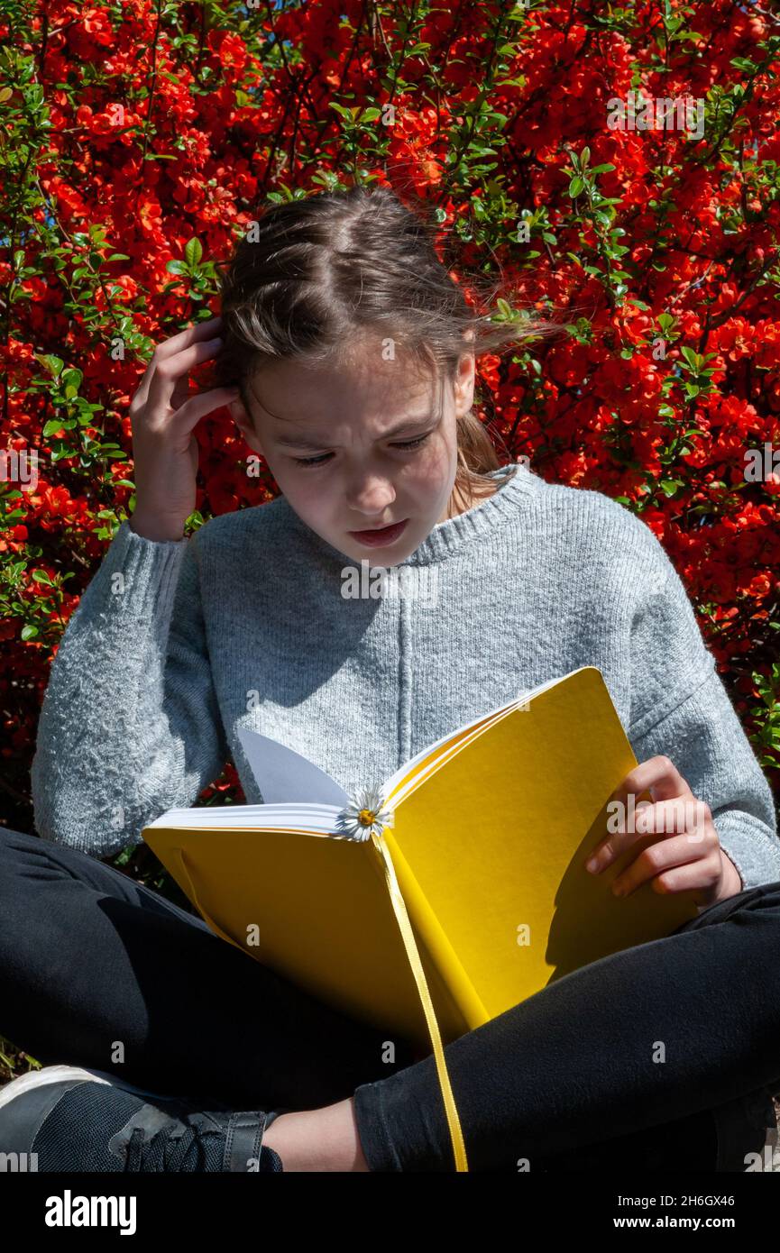 Young school age girl reading from yellow textbook in park against ...
