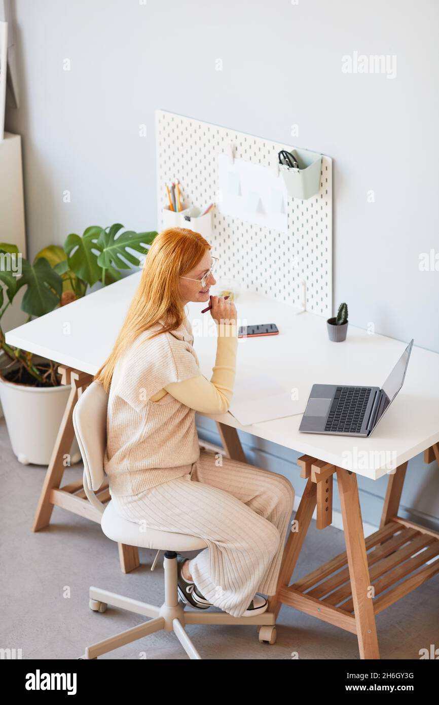 High angle portrait of adult red haired woman using laptop while ...
