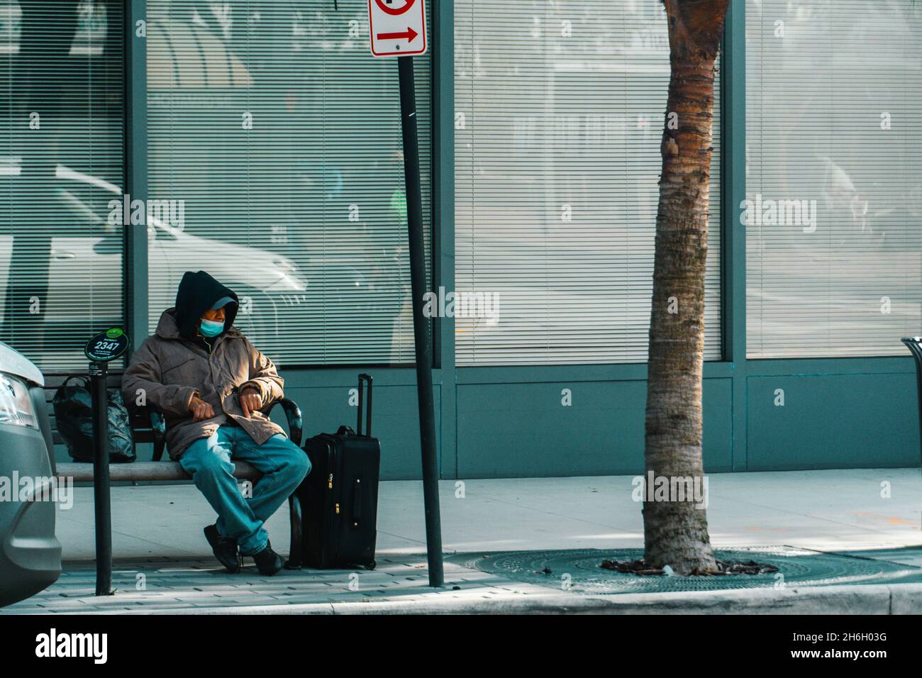 Man waiting at a bus stop in the cold with his hood up and his covid ...