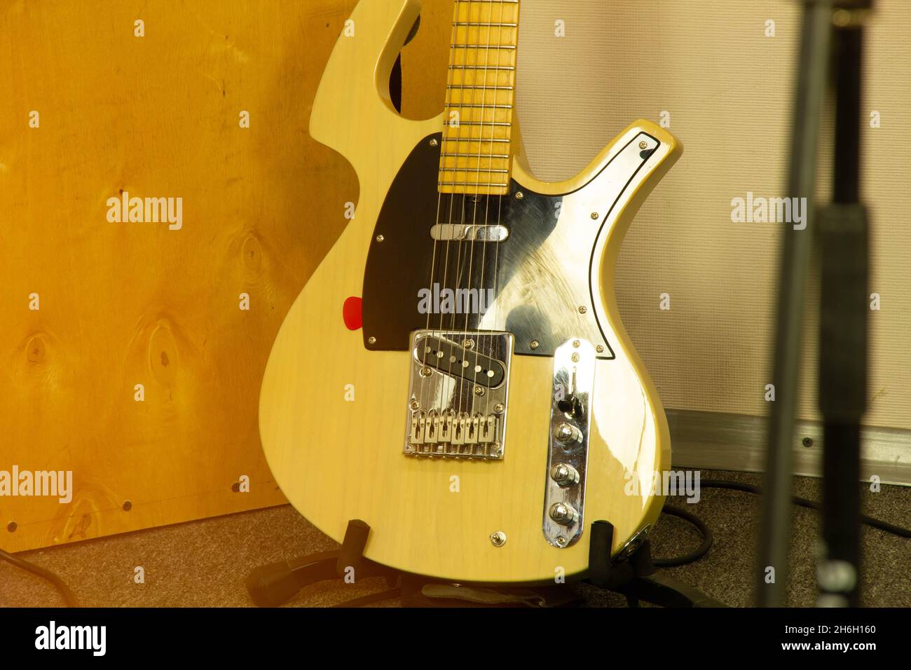 A yellow electric guitar stands against a wall in a professional music studio. Designer stringed ...
