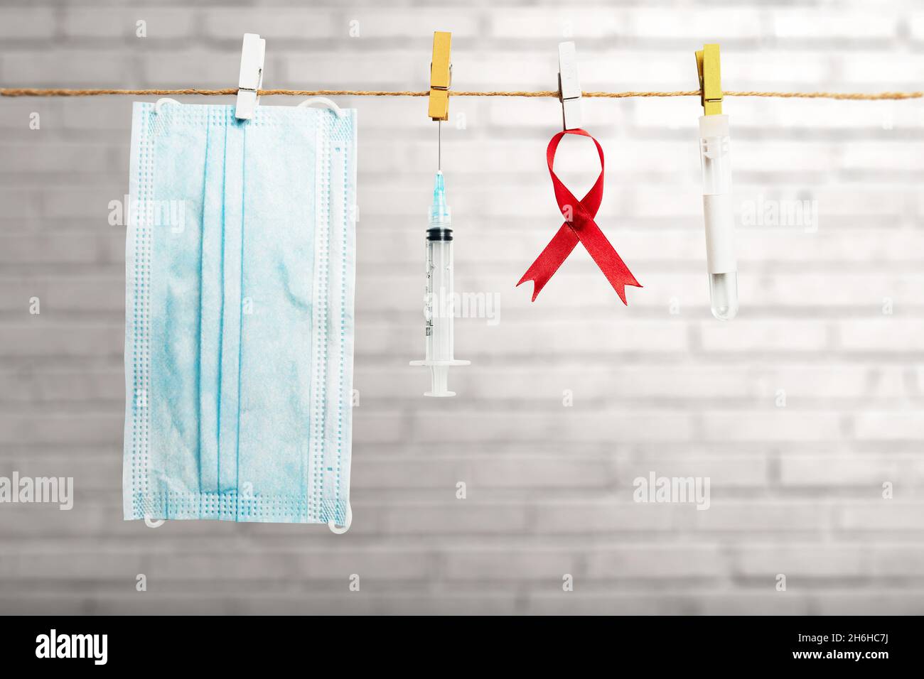 Red ribbon, syringe, and face mask hanging on the rope with brick wall ...
