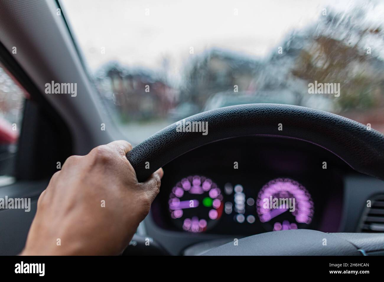 Driver's hands on steering wheel inside of a car. Driving in a rainy ...