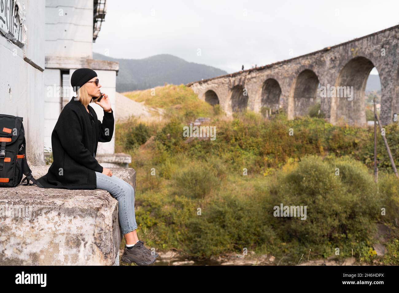 Girl traveler sitting in front of the old stone arch bridge, tourist ...