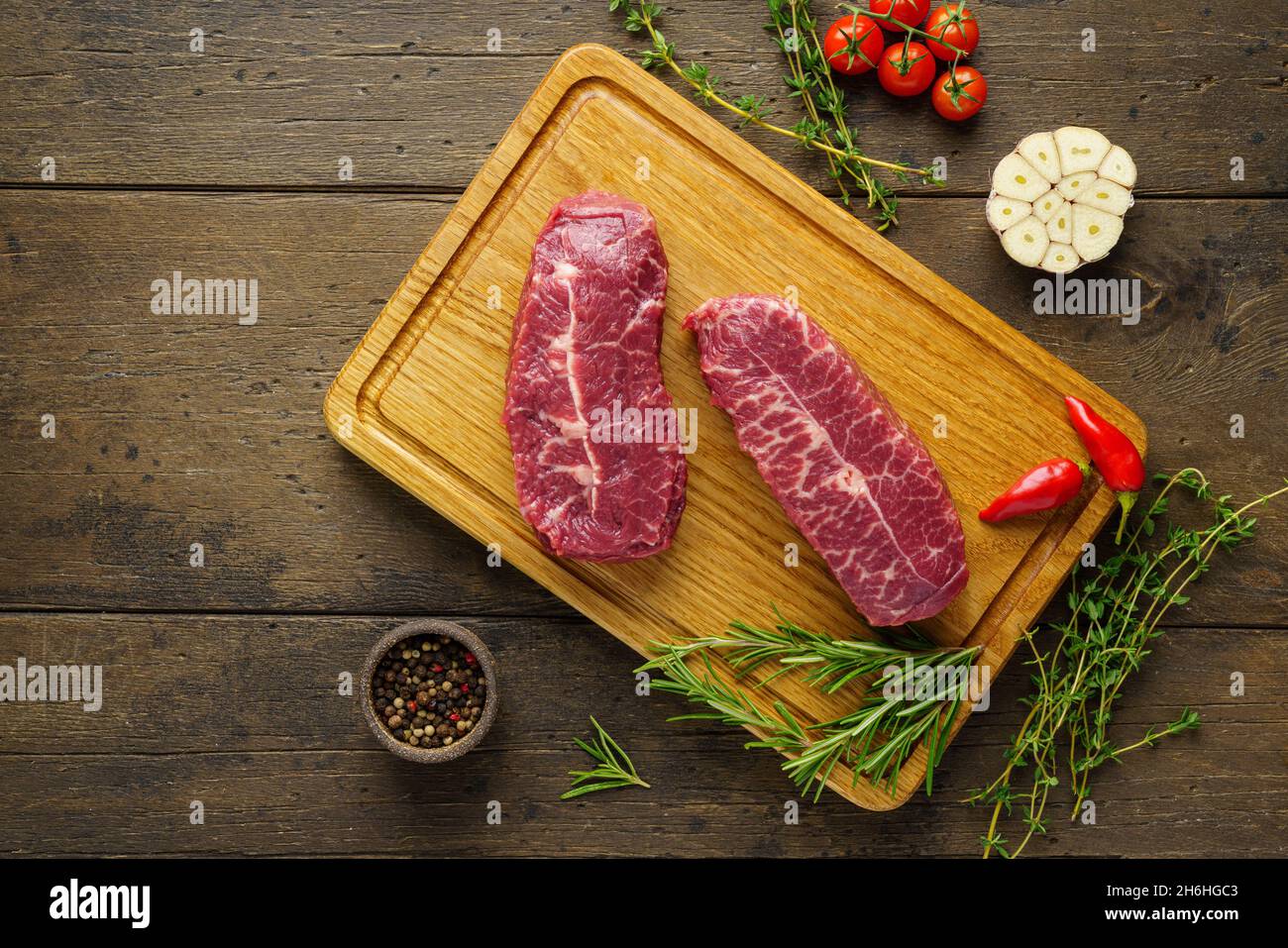 Above of two raw top blade beef steak on wood board with seasonings and ...