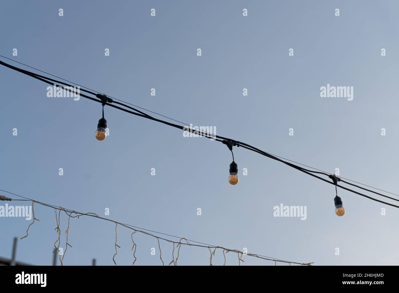 Black electricity wire with hanging lightbulbs against a bright sky ...