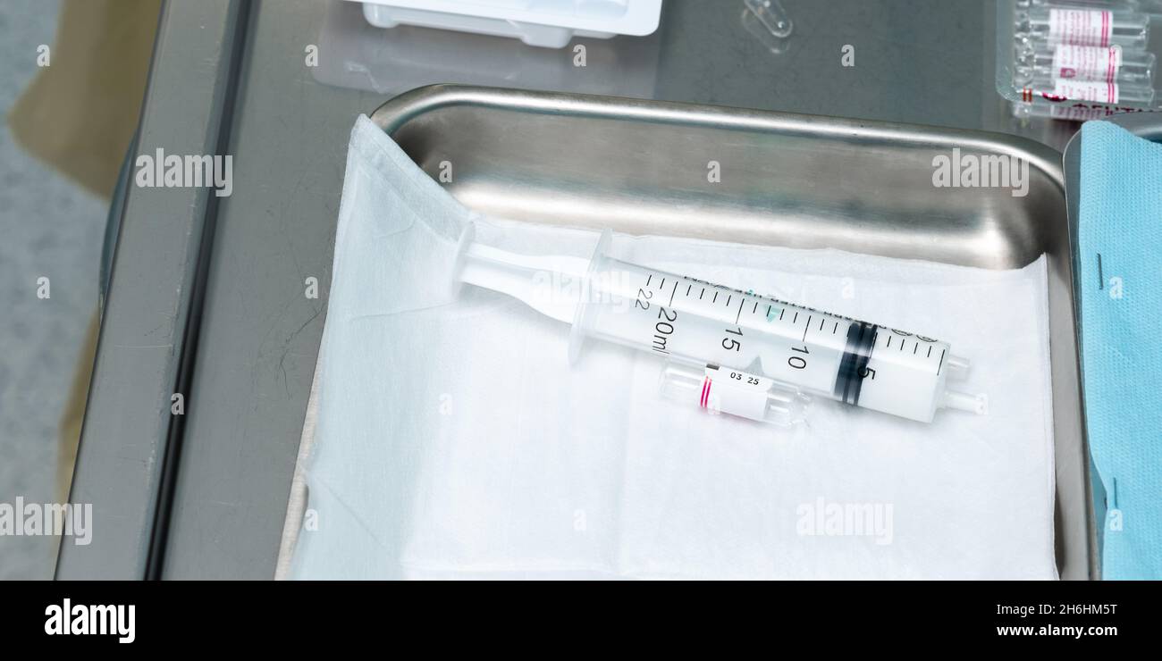 A used syringe and an empty glass ampoule opened lie in a metal cuvette ...