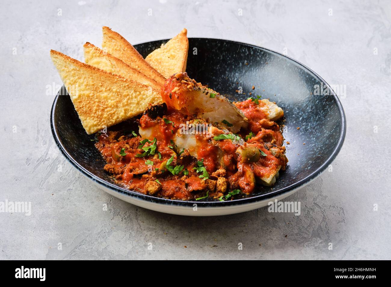 Fried zander served with steamed tomato, onion and olive sauce on a ...
