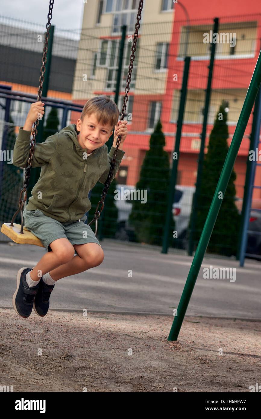 Kids play on the playground. Happy laughing boy have fun swinging and ...