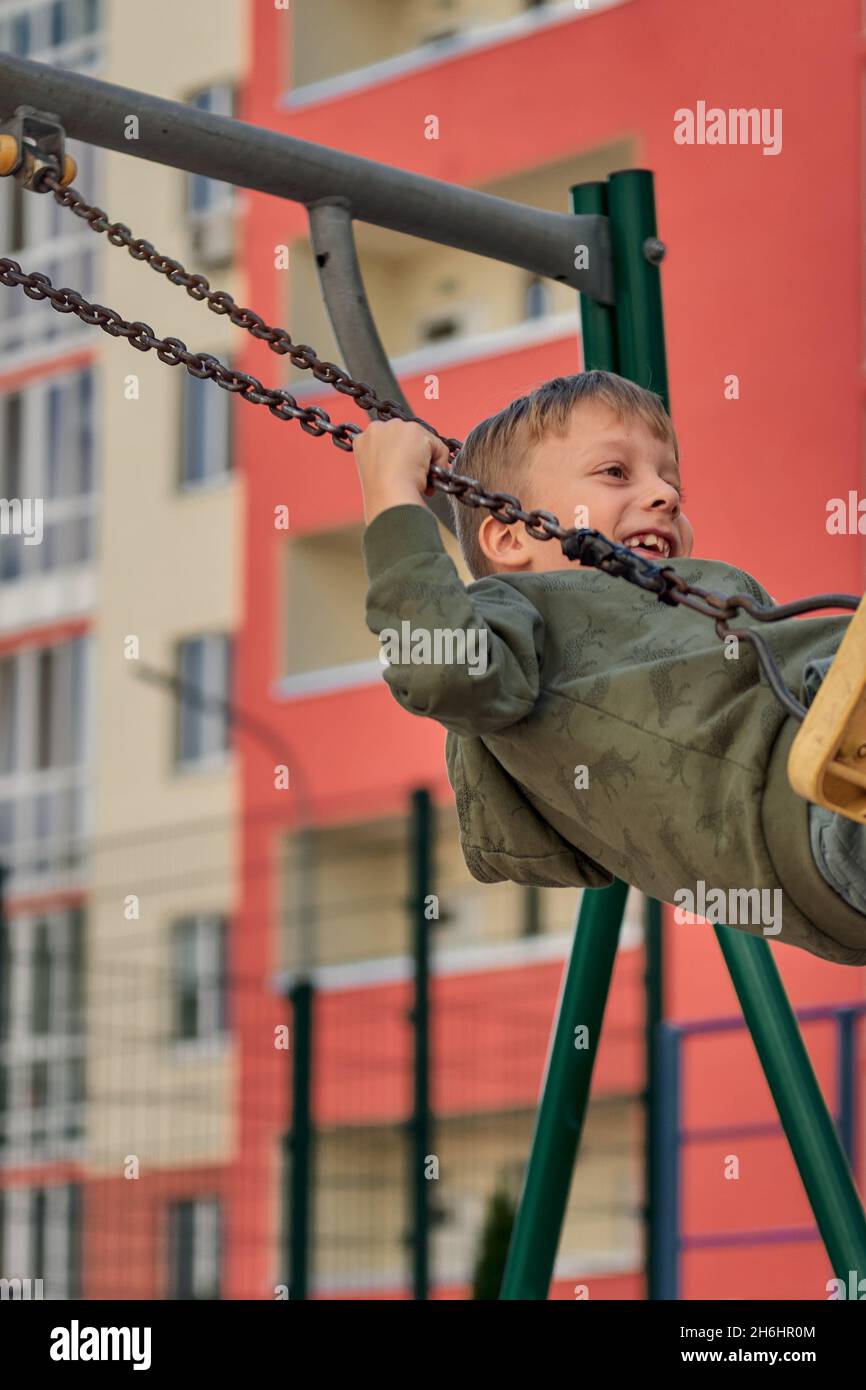 Kids play on the playground. Happy laughing boy have fun swinging and ...
