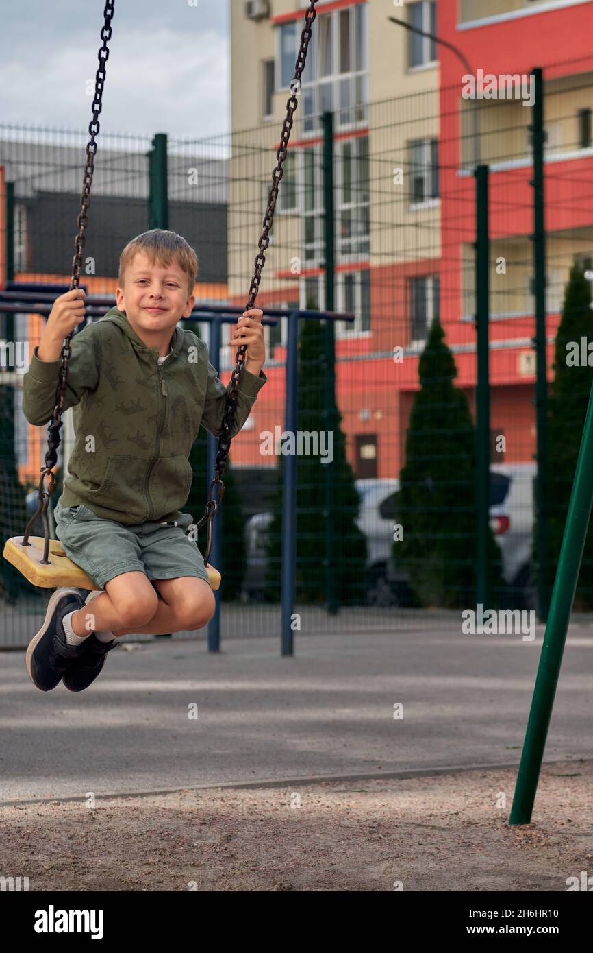 Kids play on the playground. Happy laughing boy have fun swinging and ...