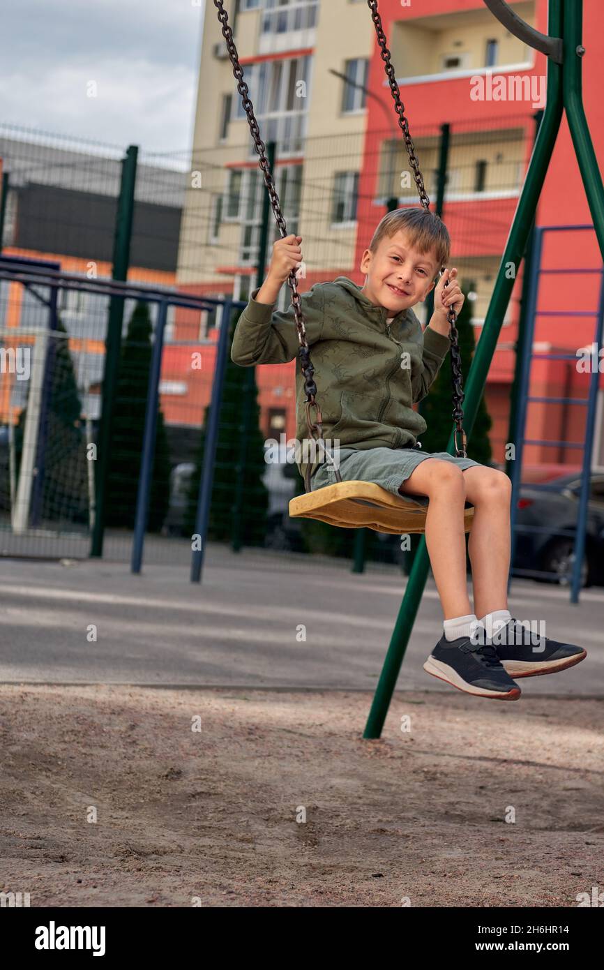 Kids play on the playground. Happy laughing boy have fun swinging and ...