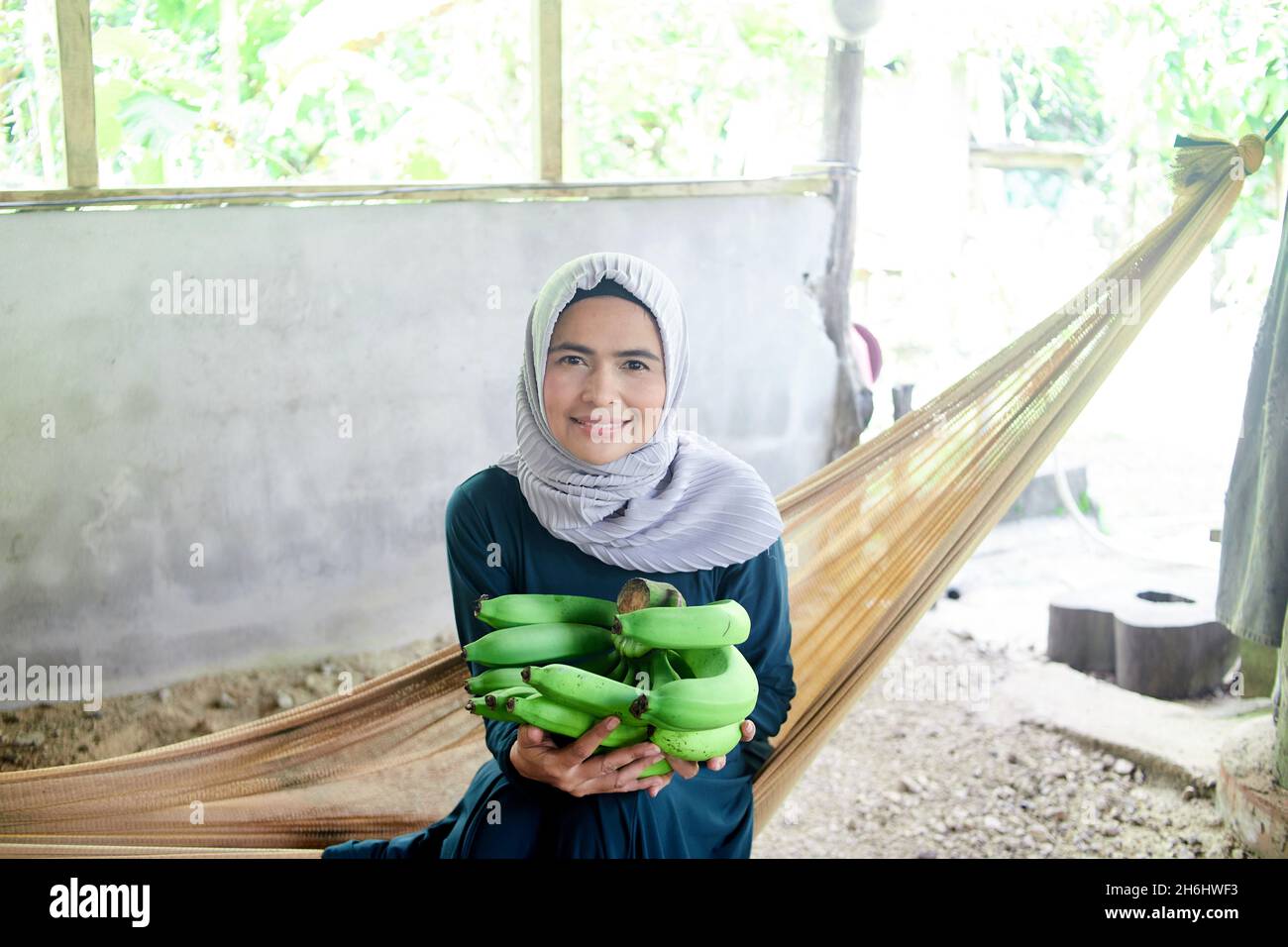 Muslim woman sitting on net cradle and holding bunch of green banana ...