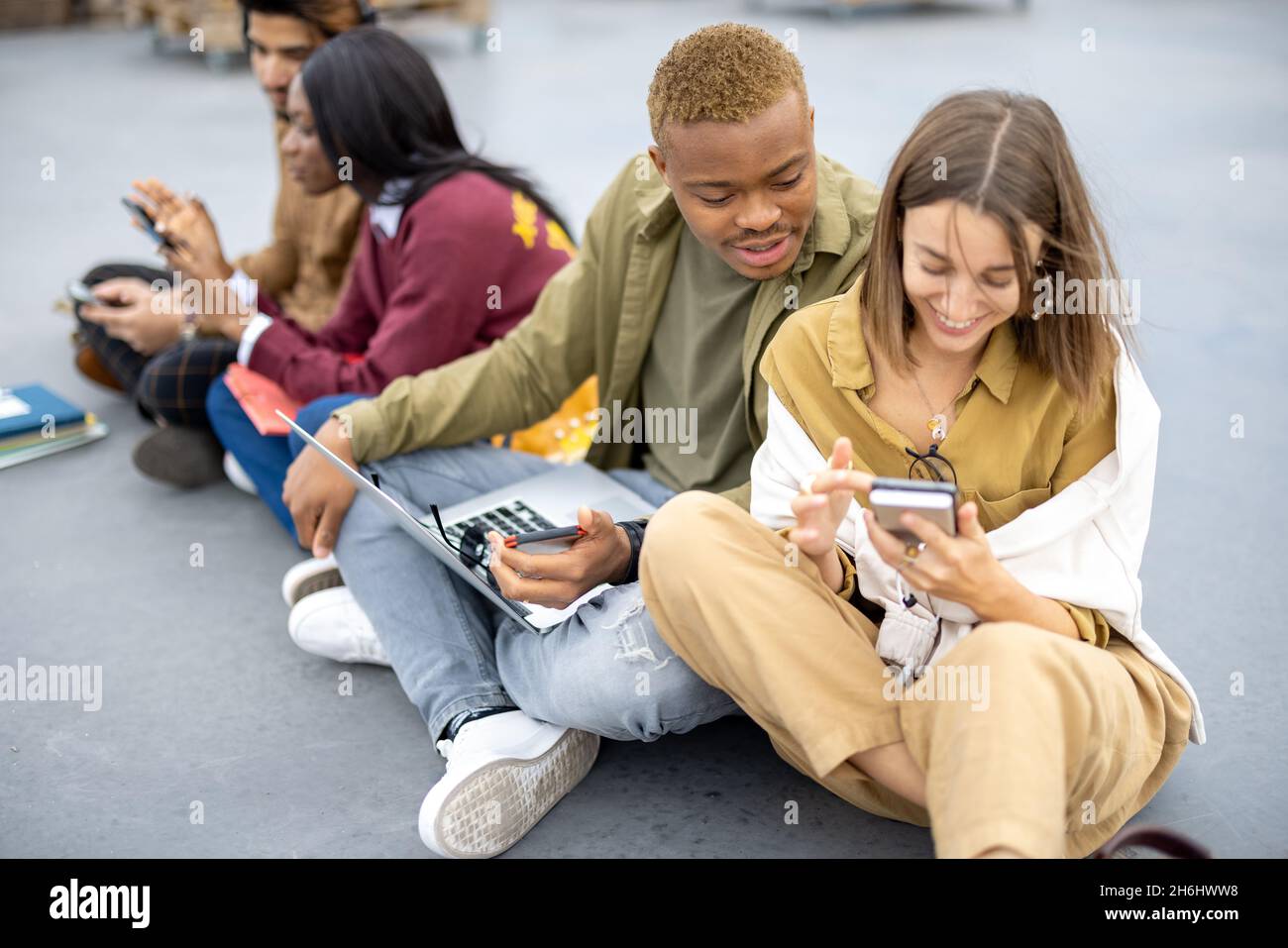 Students sitting and using gadgets on asphalt Stock Photo - Alamy