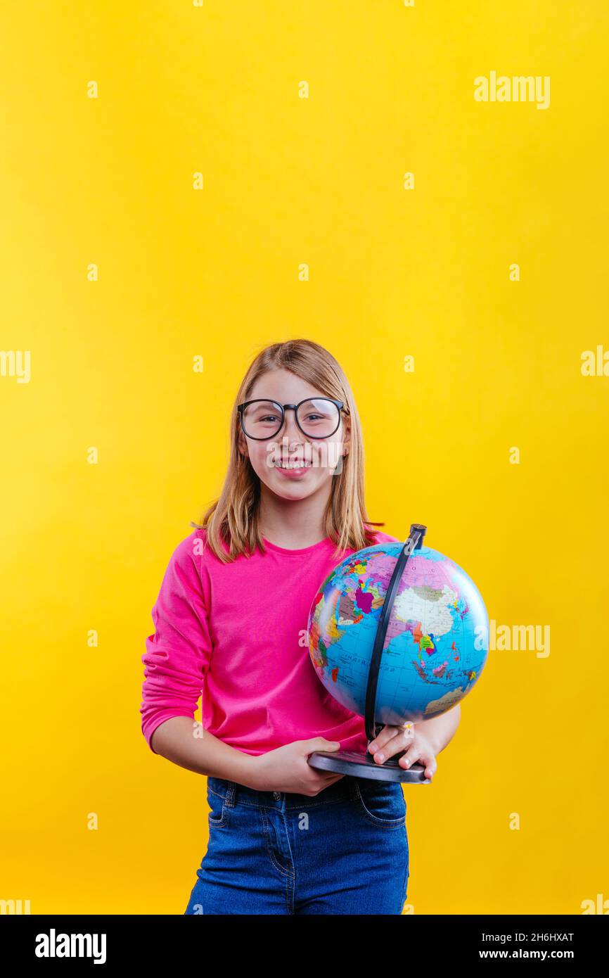 Happy blonde hair schoolgirl with eye glasses holding globe on yellow ...