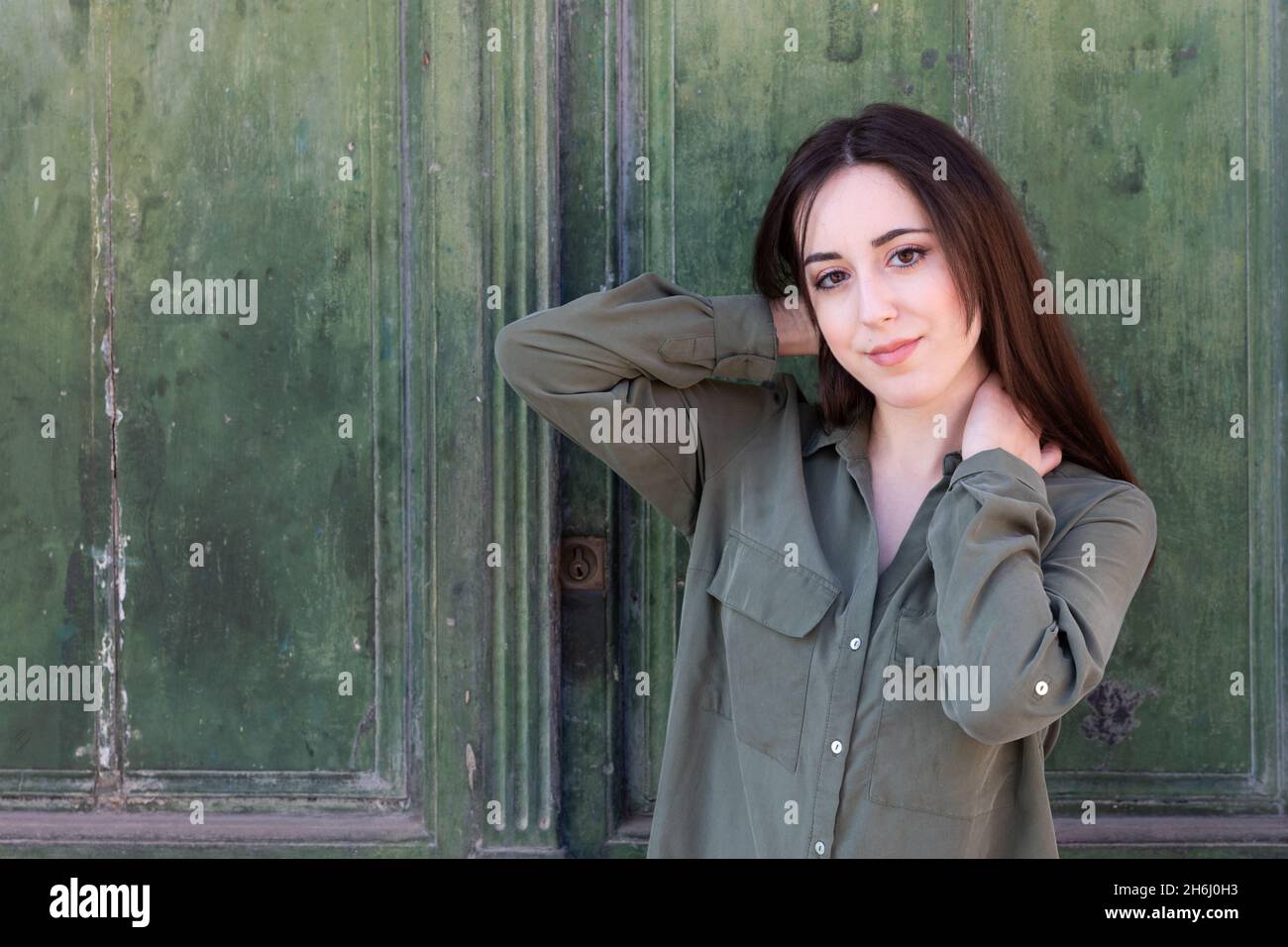 Young Brunette stylish lady posing in a green old door background Stock Photo - Alamy