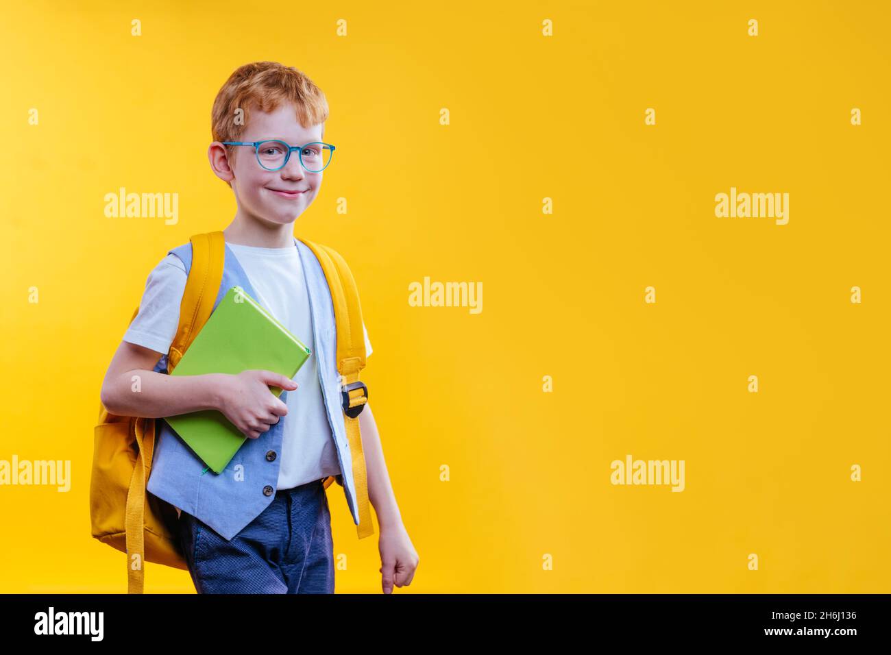Happy teenager boy holding backpack and book looking at camera. Studio ...