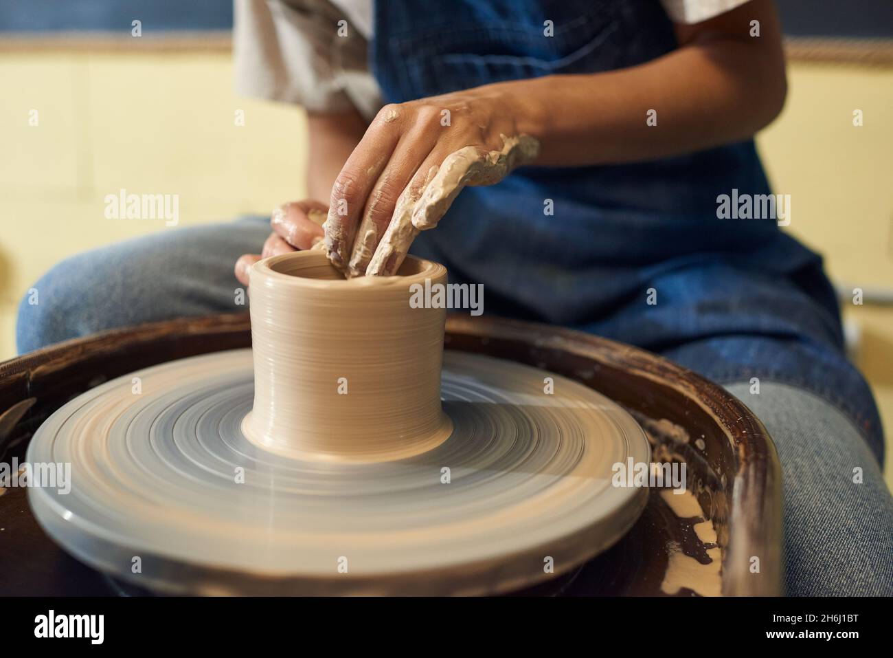 Hands of young female potter sitting by rotating pottery wheel while ...