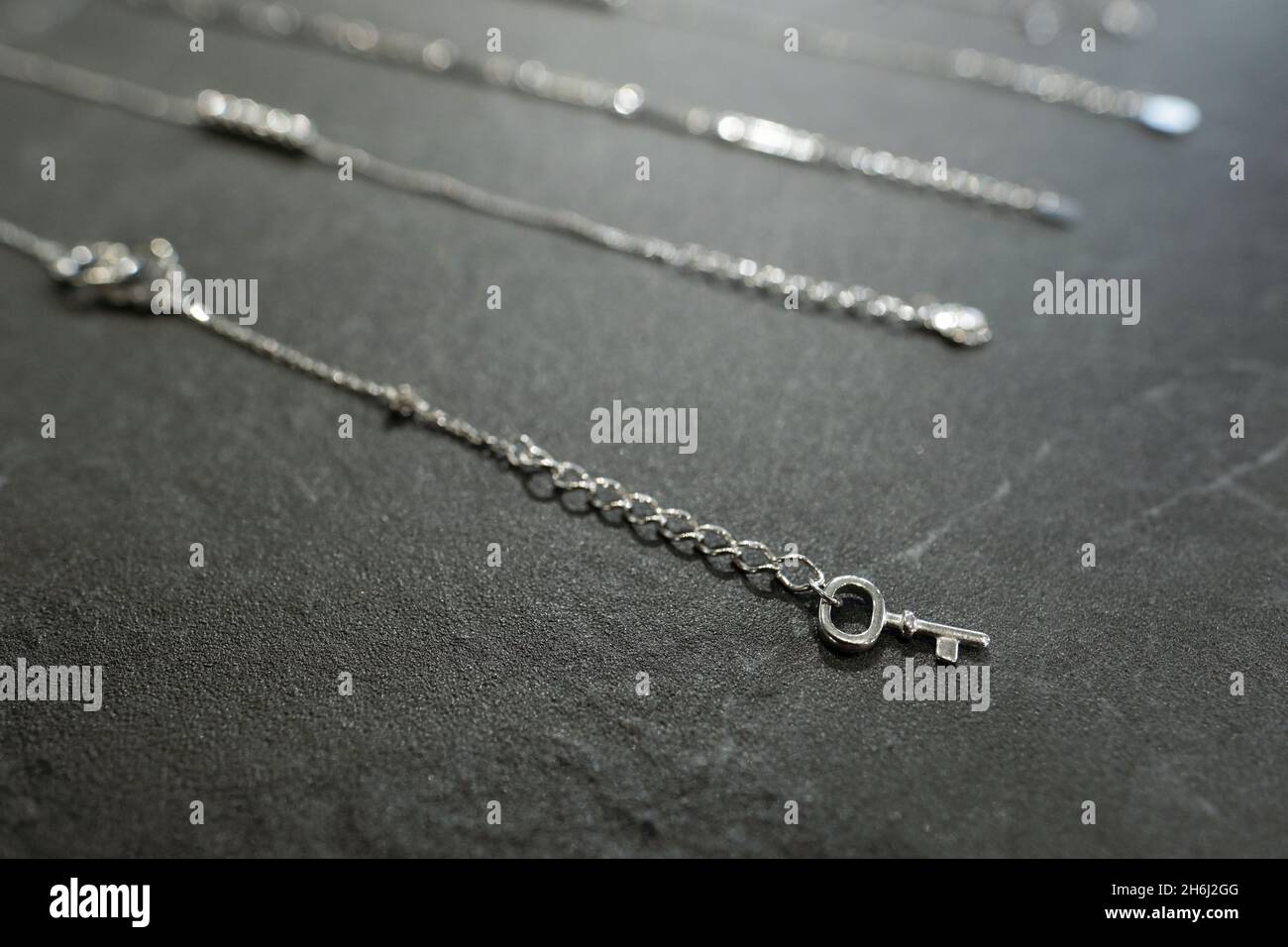 Silver necklace or bracelet with tiny decorative key over dark grey ...