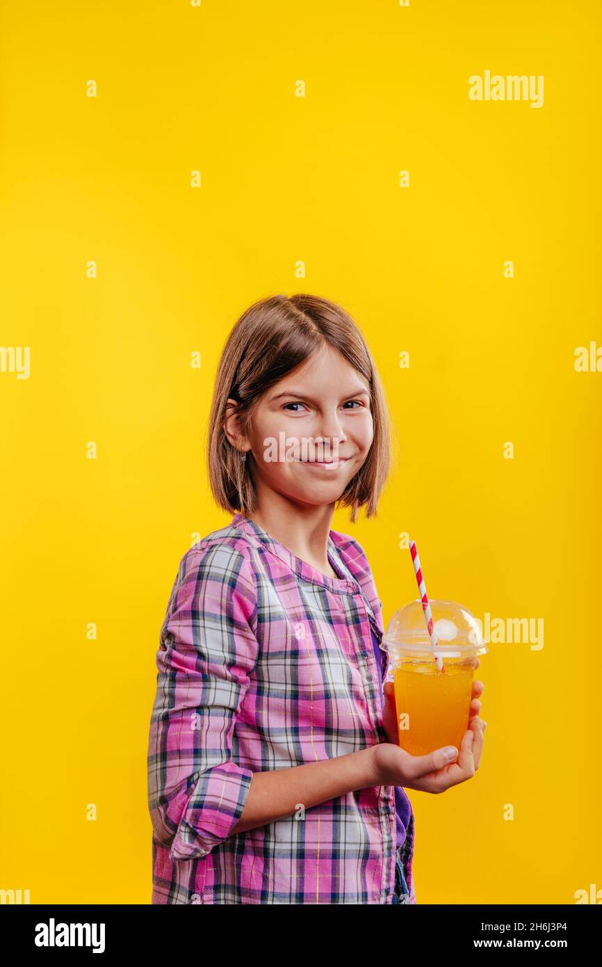 Teenager girl drinking orange juice. Studio portrait on yellow ...