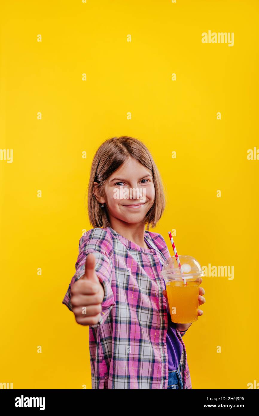 Teenager girl drinking orange juice. Studio portrait on yellow ...