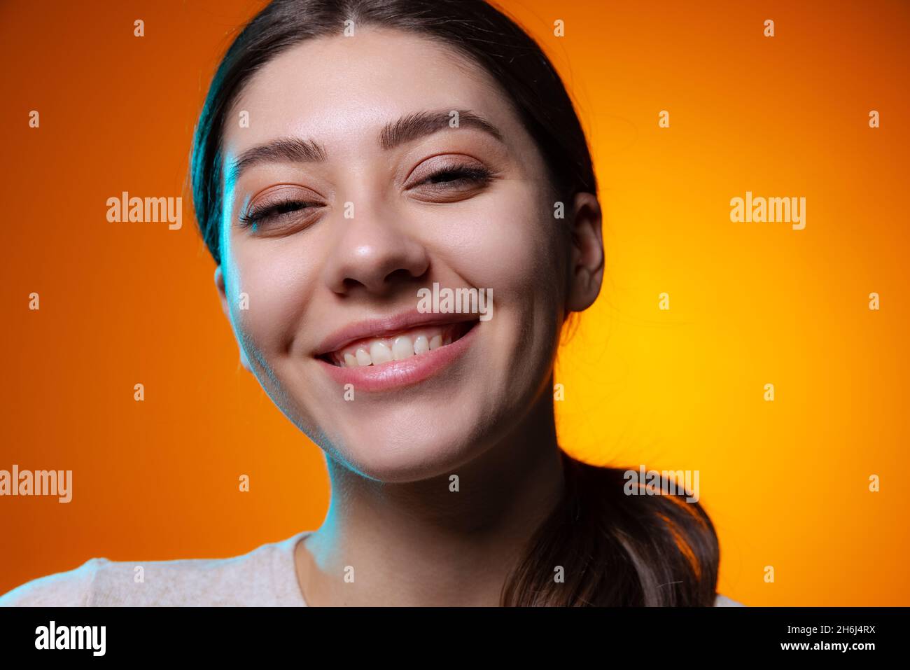 Close-up portrait of young beautiful smiling girl isolated on yellow brown studio background in ...
