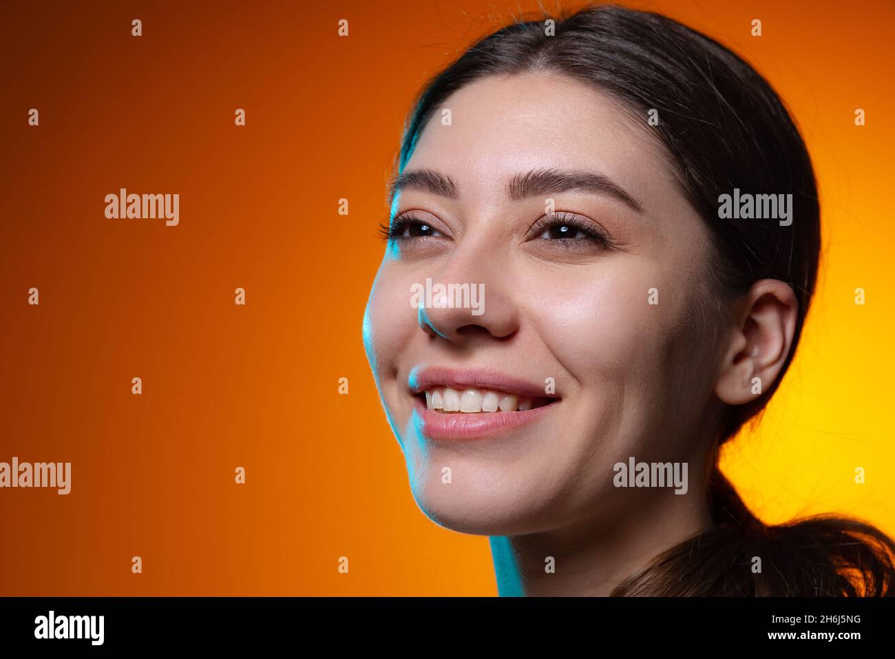 Close-up portrait of young beautiful smiling girl isolated on yellow brown studio background in ...