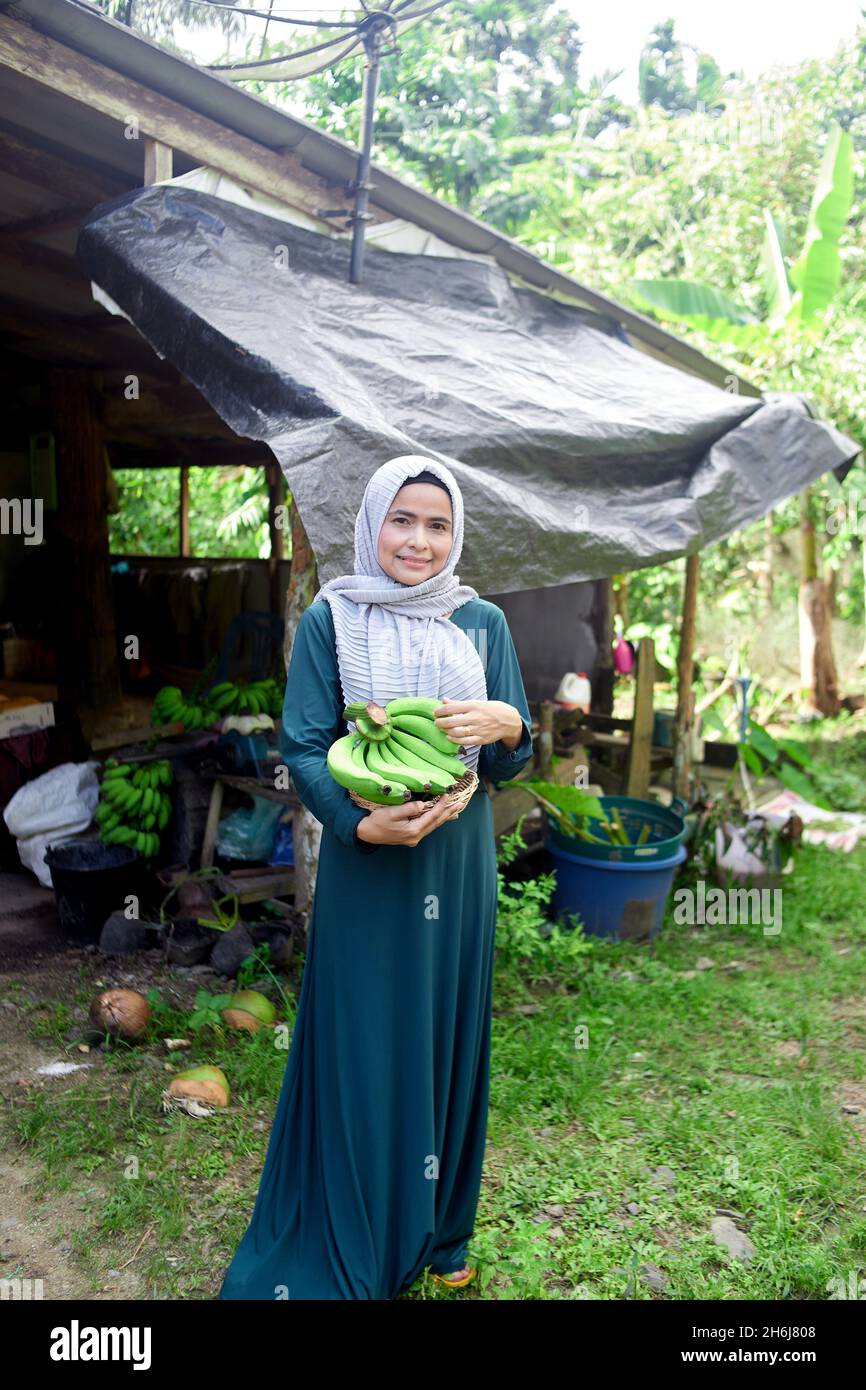 Muslim woman in hijab standing and holding raw banana in home area ...