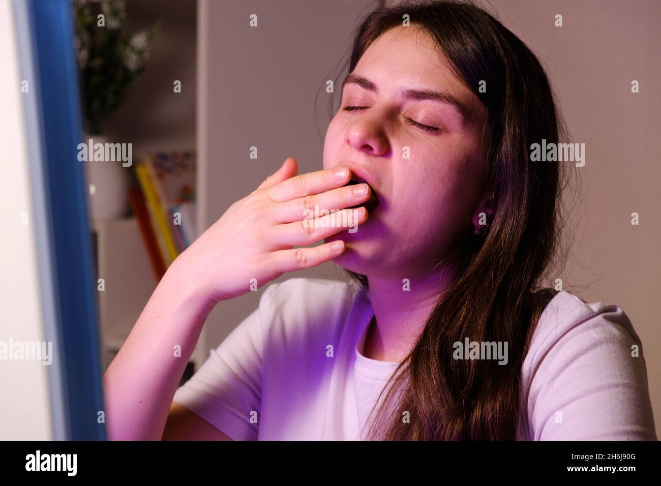 A woman yawns sitting in front of a computer or TV screen. Boring movie ...