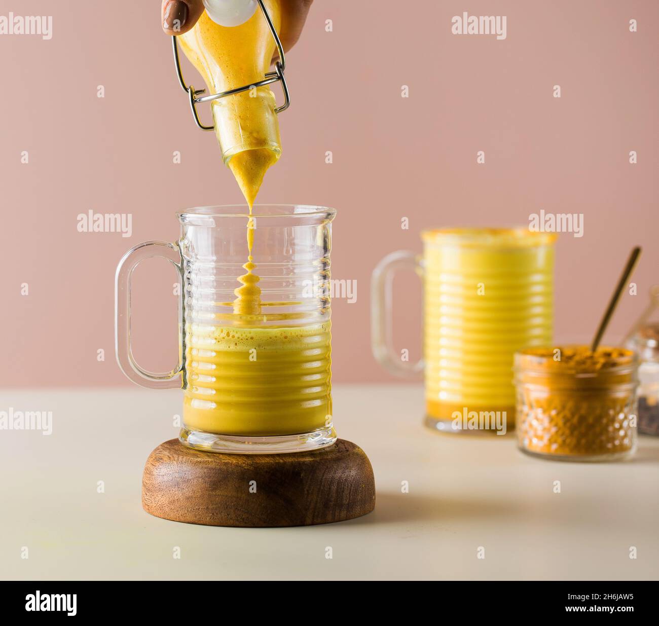 Golden latte with turmeric poured over pink background. Moon milk for ...