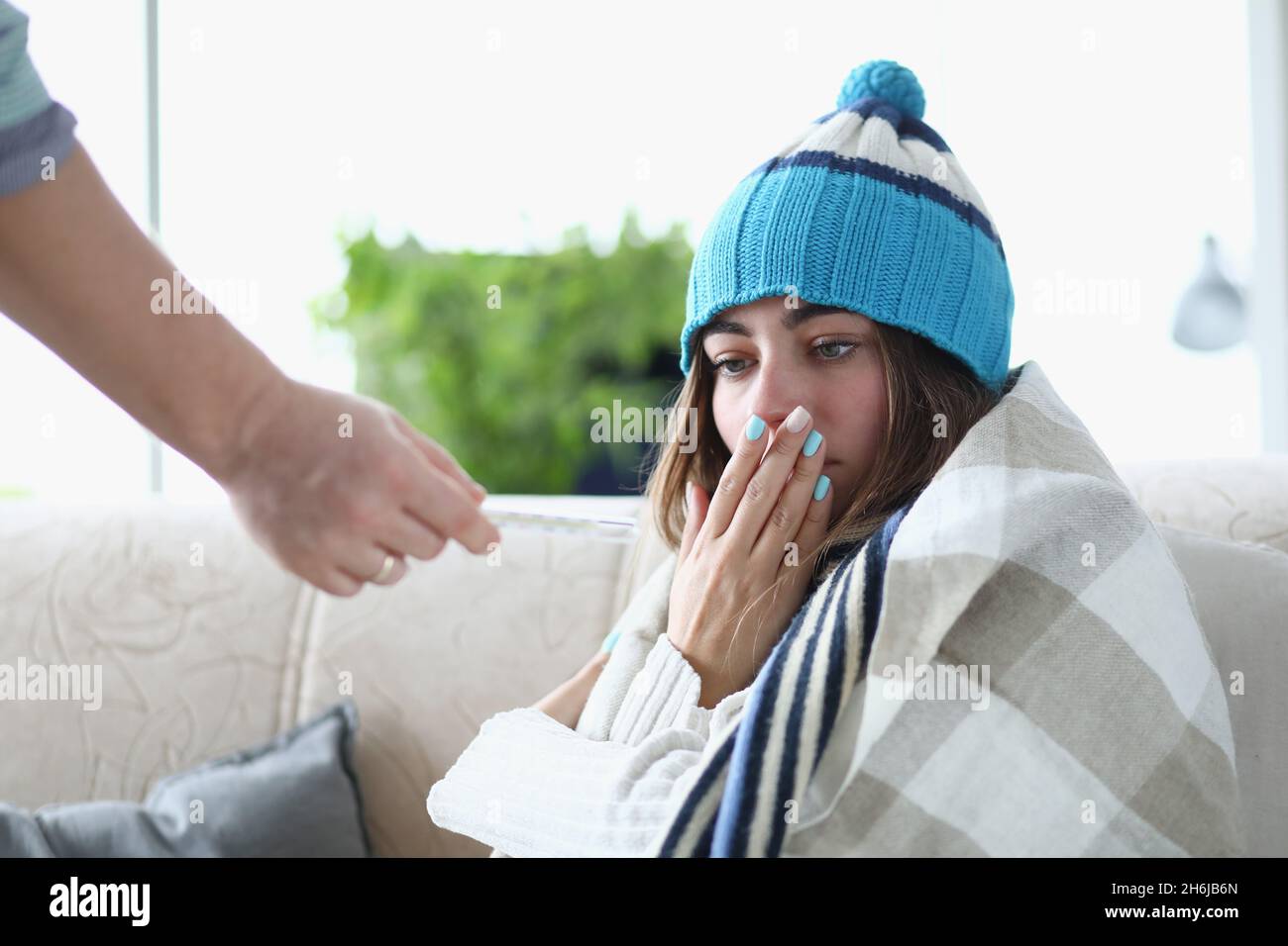 Young woman in hat and plaid with chills looks at thermometer with high ...