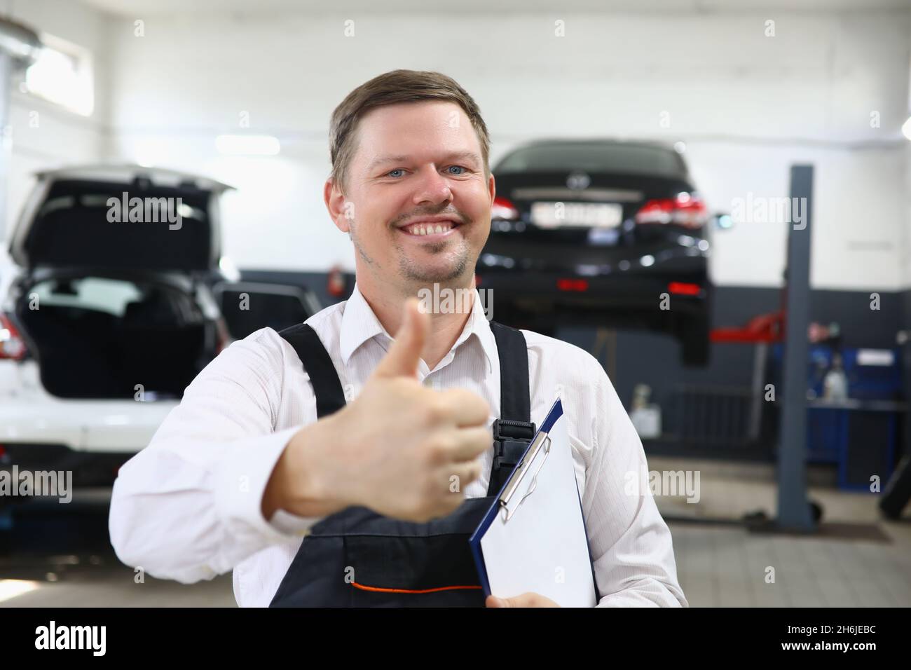 Portrait of a young smiling car mechanic holding thumbs up in car ...