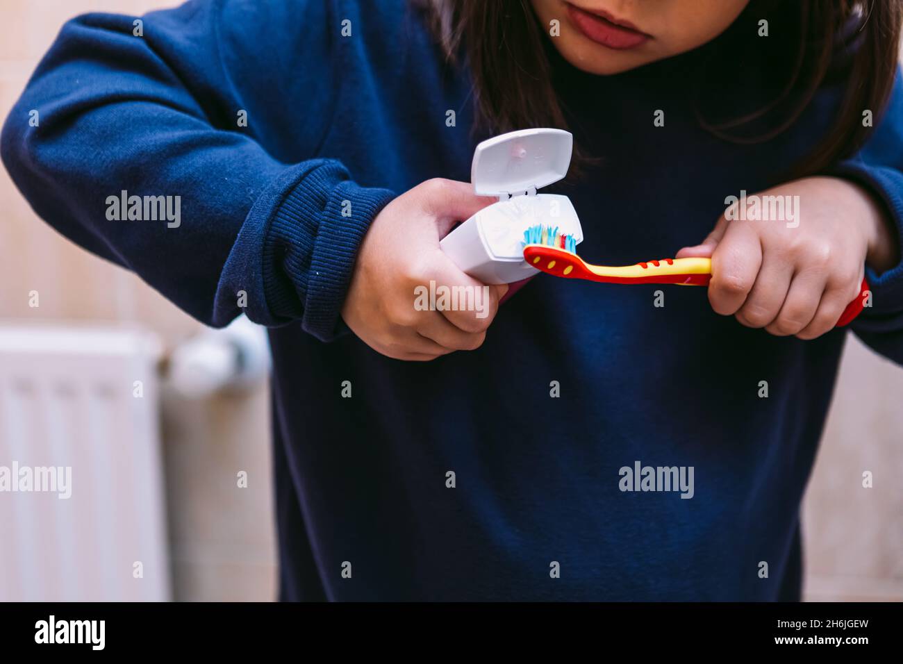 Detail of toothbrush pouring toothpaste by little girl in dark blue ...