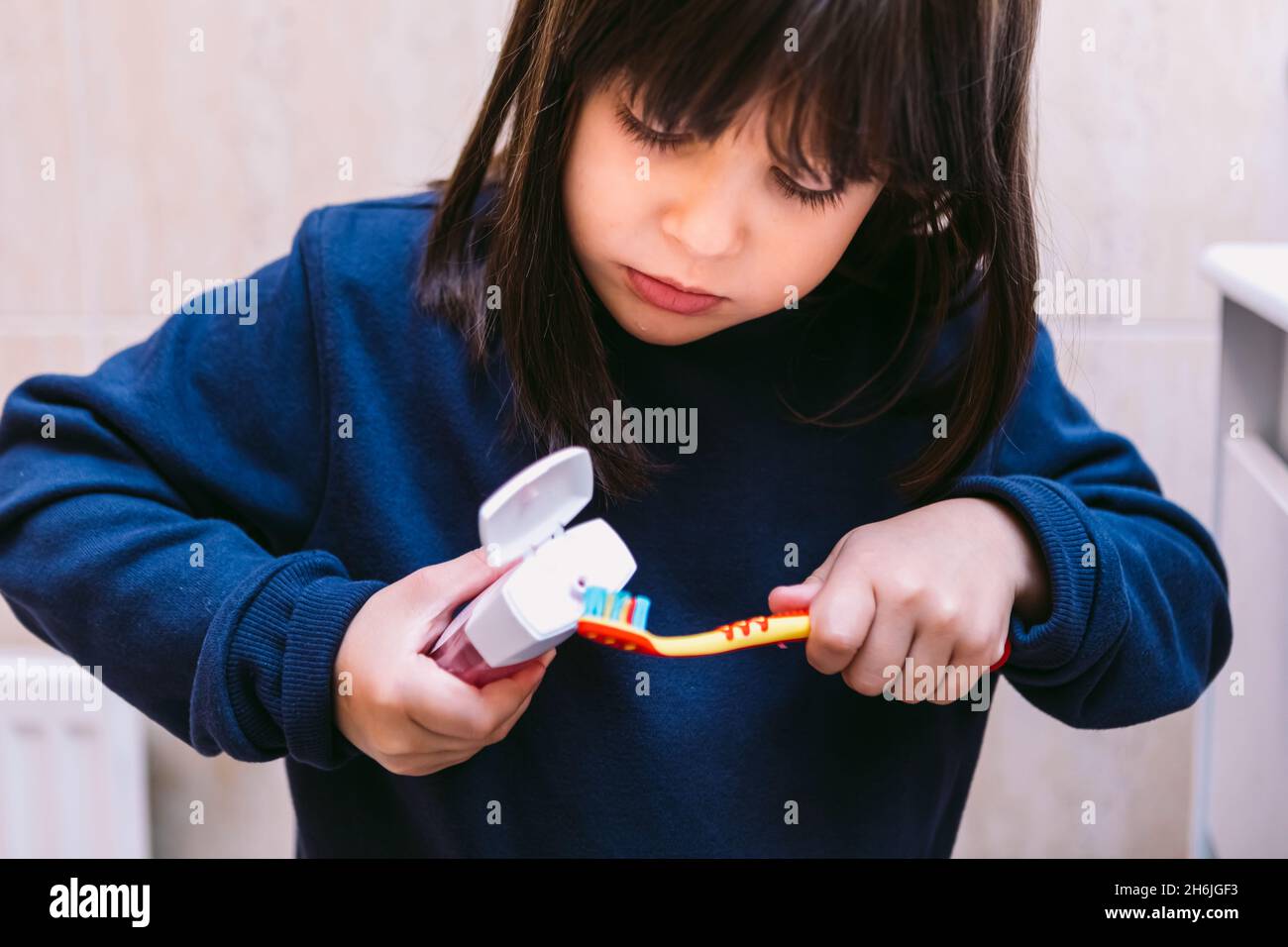 Little girl in a dark blue sweatshirt, putting toothpaste on her ...