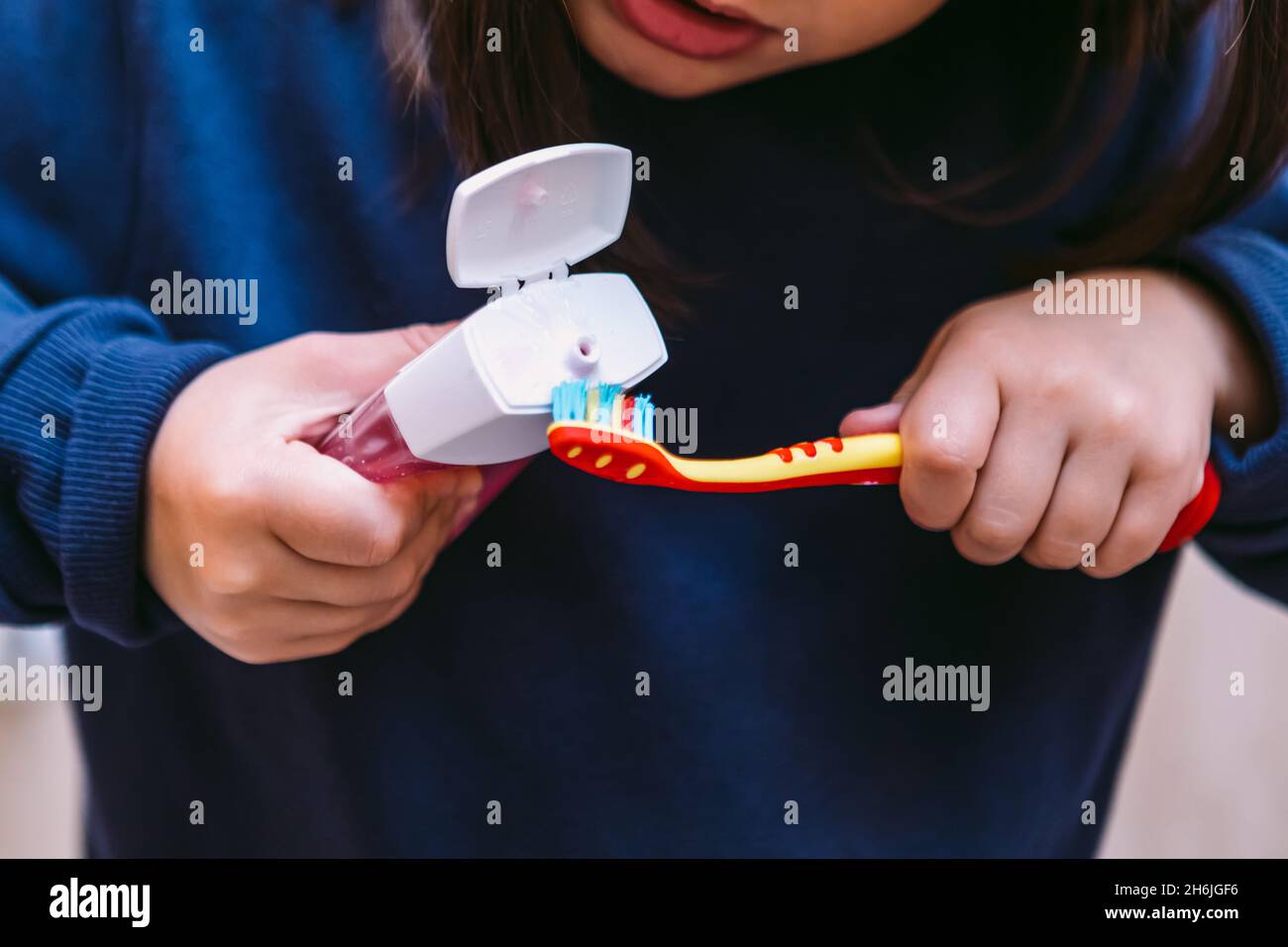 Detail of toothbrush pouring toothpaste by little girl in dark blue ...