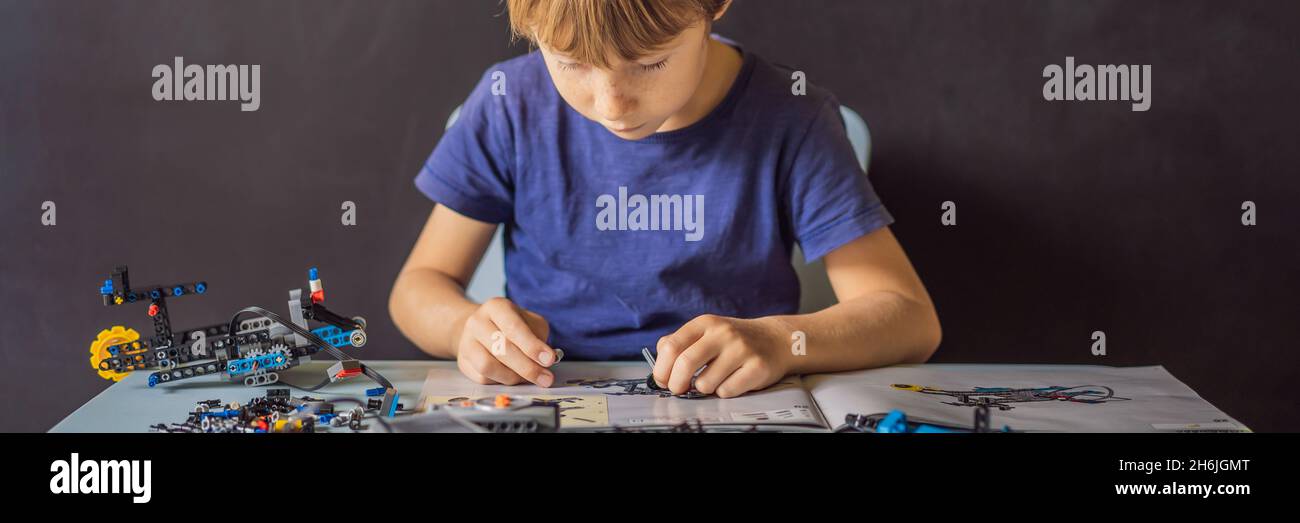 Cheerful smart schoolboy sitting at the table and constructing a ...
