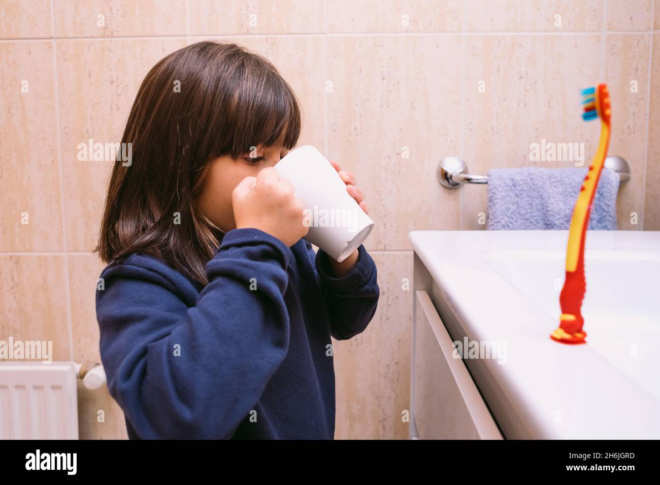 Little girl in a dark blue sweatshirt, brushing her teeth, rinsing her ...