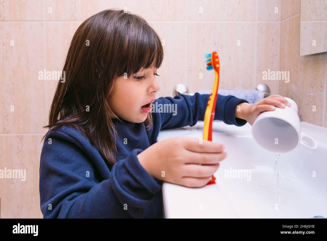 Little girl in a dark blue sweatshirt, brushing her teeth, rinsing ...
