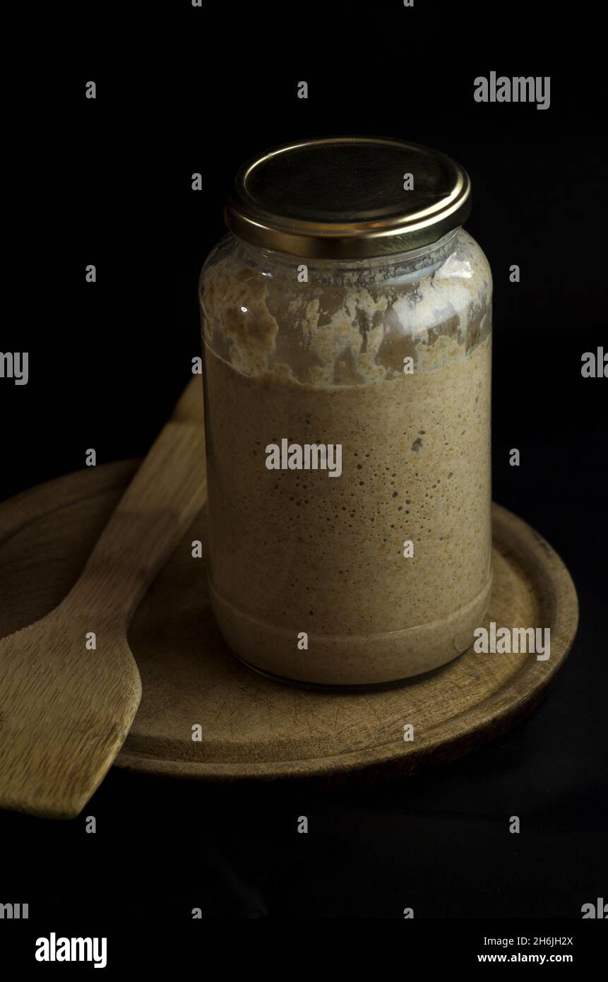 Wooden spoon and sourdough starter in a glass jar isolated on black ...
