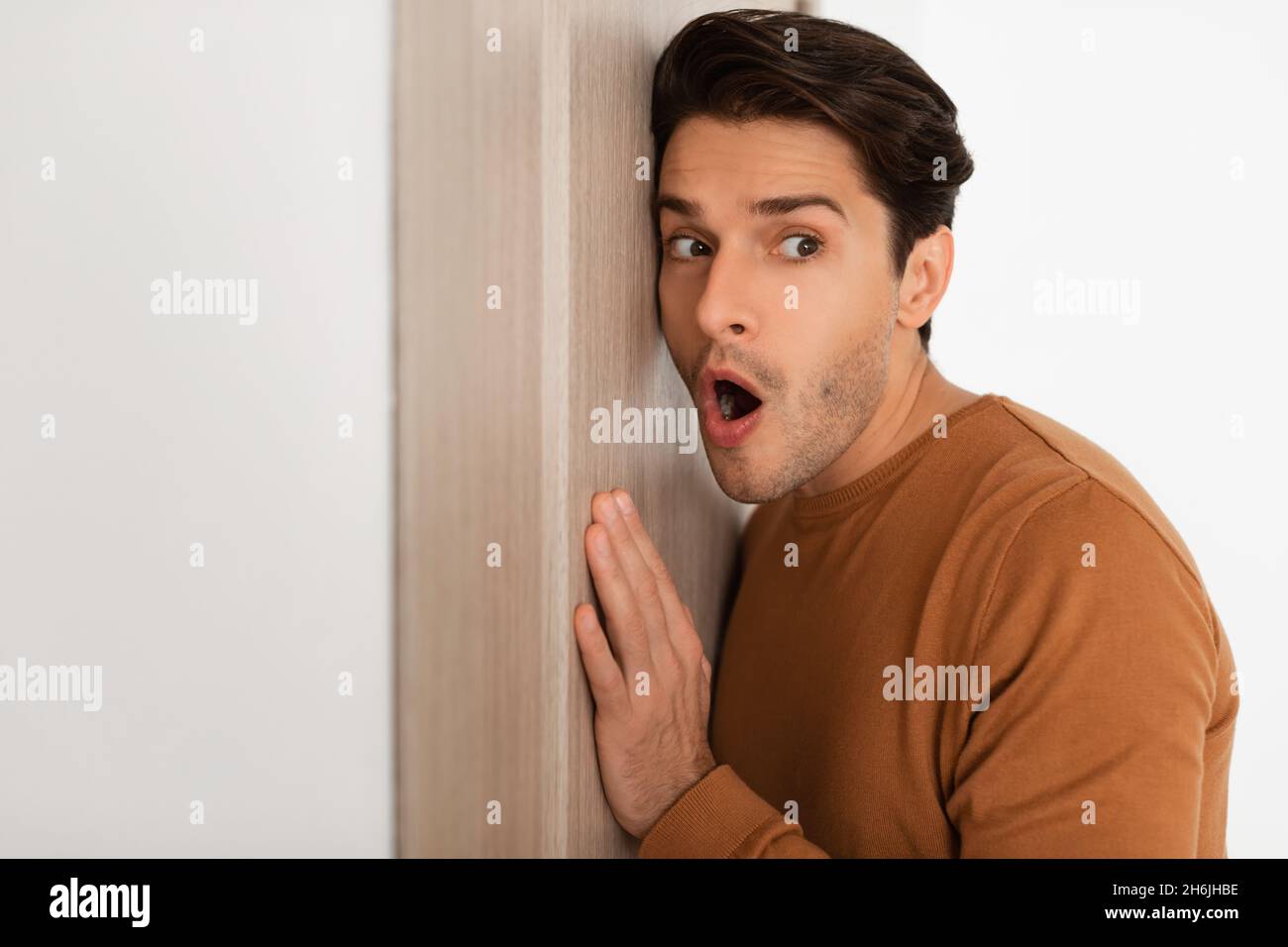 Shocked young guy listening through the door Stock Photo - Alamy