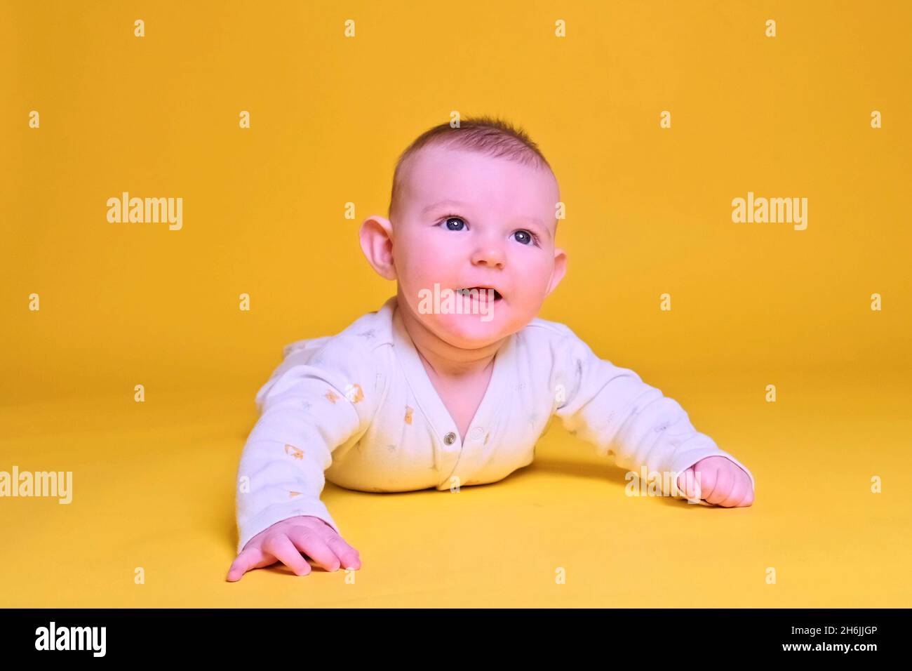 Happy infant baby boy smiling lying on his tummy, studio yellow ...