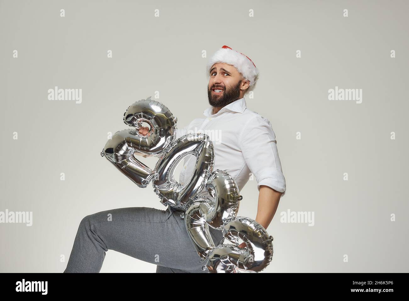 An embarrassing man with a beard in a red velvet Santa hat is holding ...