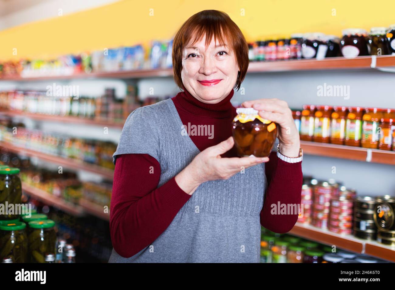 Mature cheerful female in the shop holding preserved jar of jam Stock ...