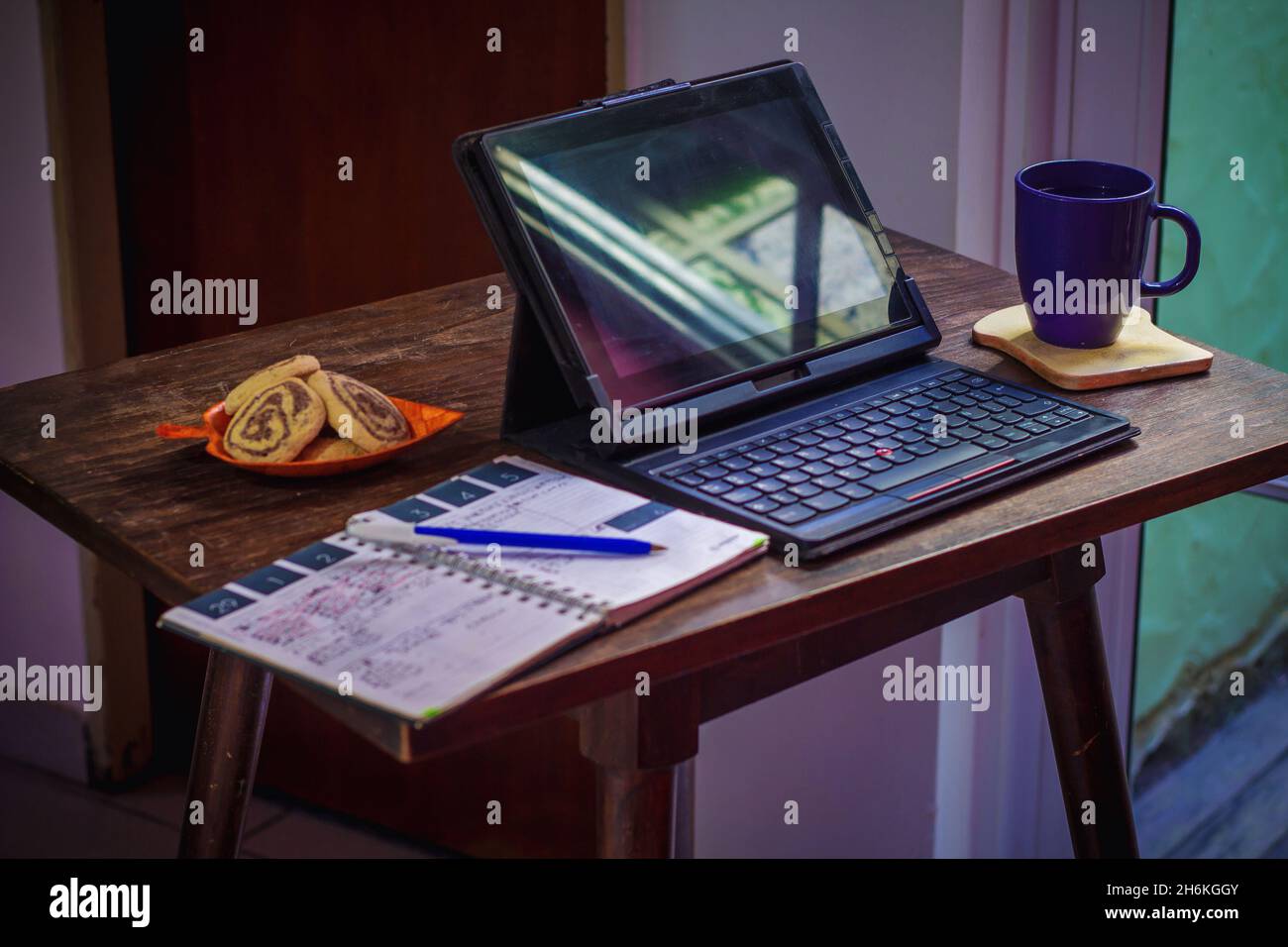 Notebook beside pastries, pen, and a cup of coffee on a wooden table ...