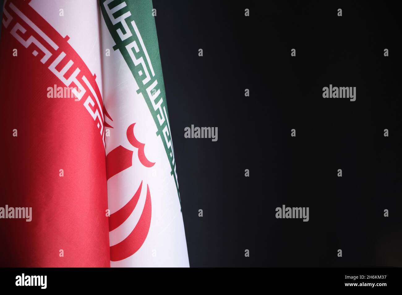 Standing flag of Iran illuminated by daylight on a dark background ...