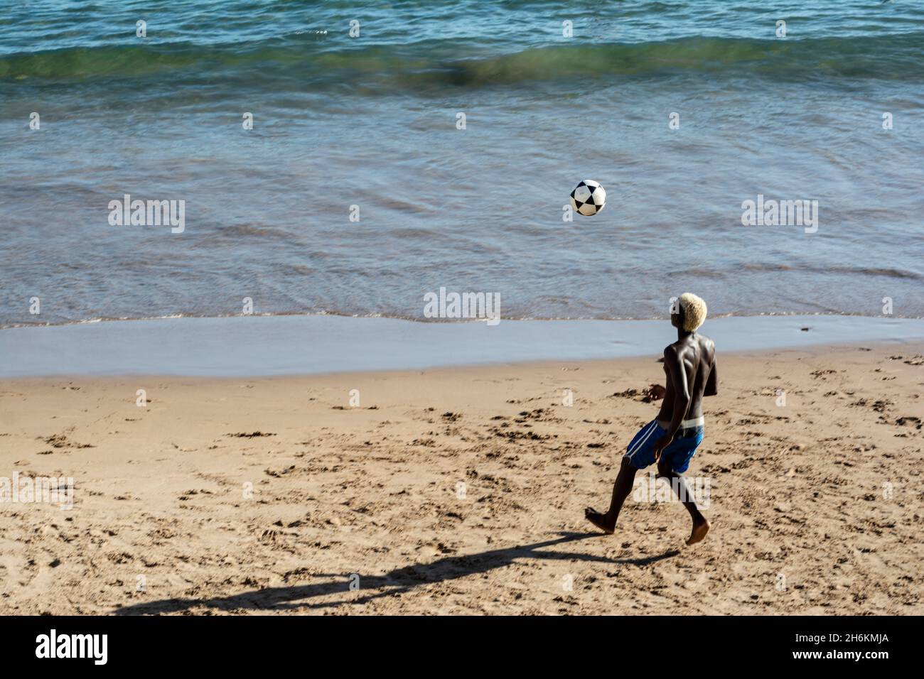 Young model playing sand football on the beach under strong summer sun ...