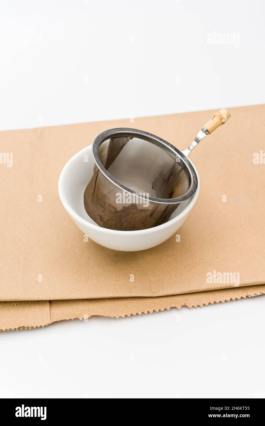 metal tea strainer in a white stoneware bowl and paper bag on a white ...