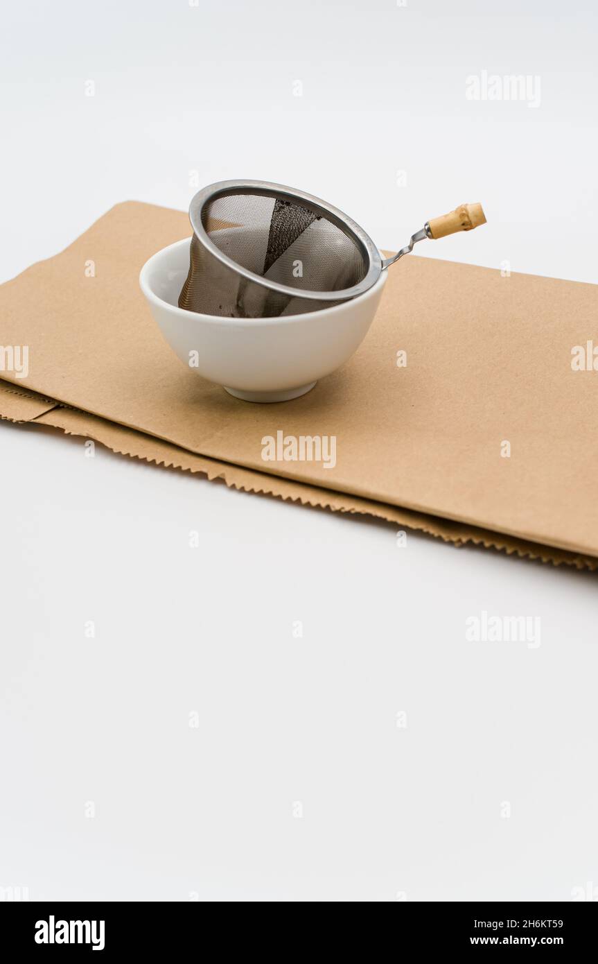 metal tea strainer in a white stoneware bowl and paper bag on a white ...