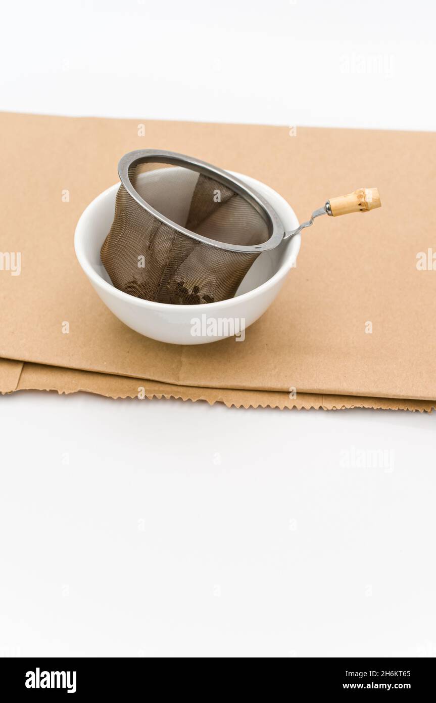metal tea strainer in a white stoneware bowl and paper bag on a white ...