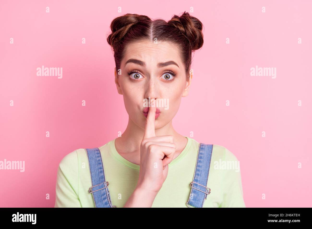 Photo portrait girl in overall keeping secret finger near lips isolated ...